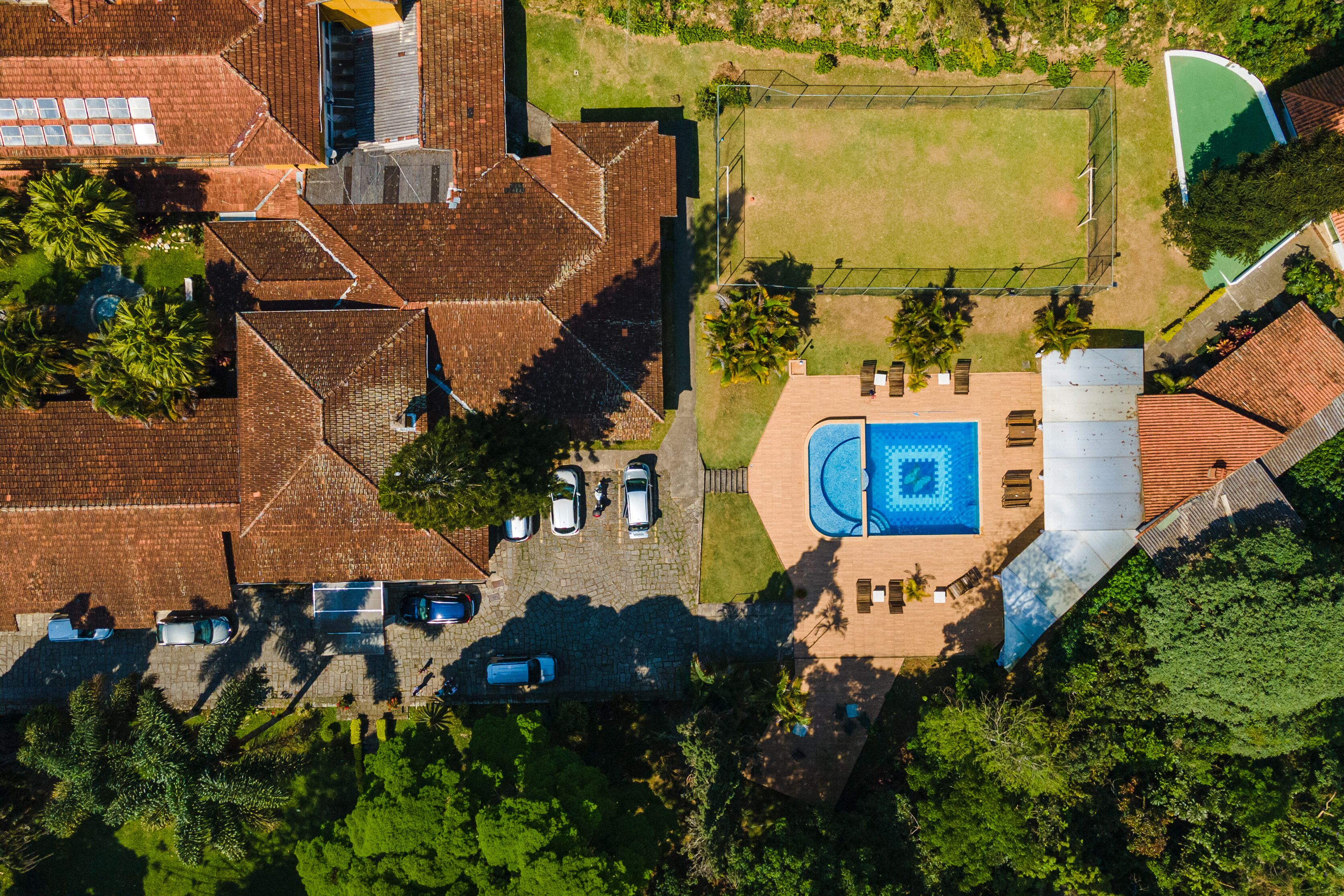 Vista aérea de uma propriedade residencial com piscina, quadra de tênis e área de varanda coberta.