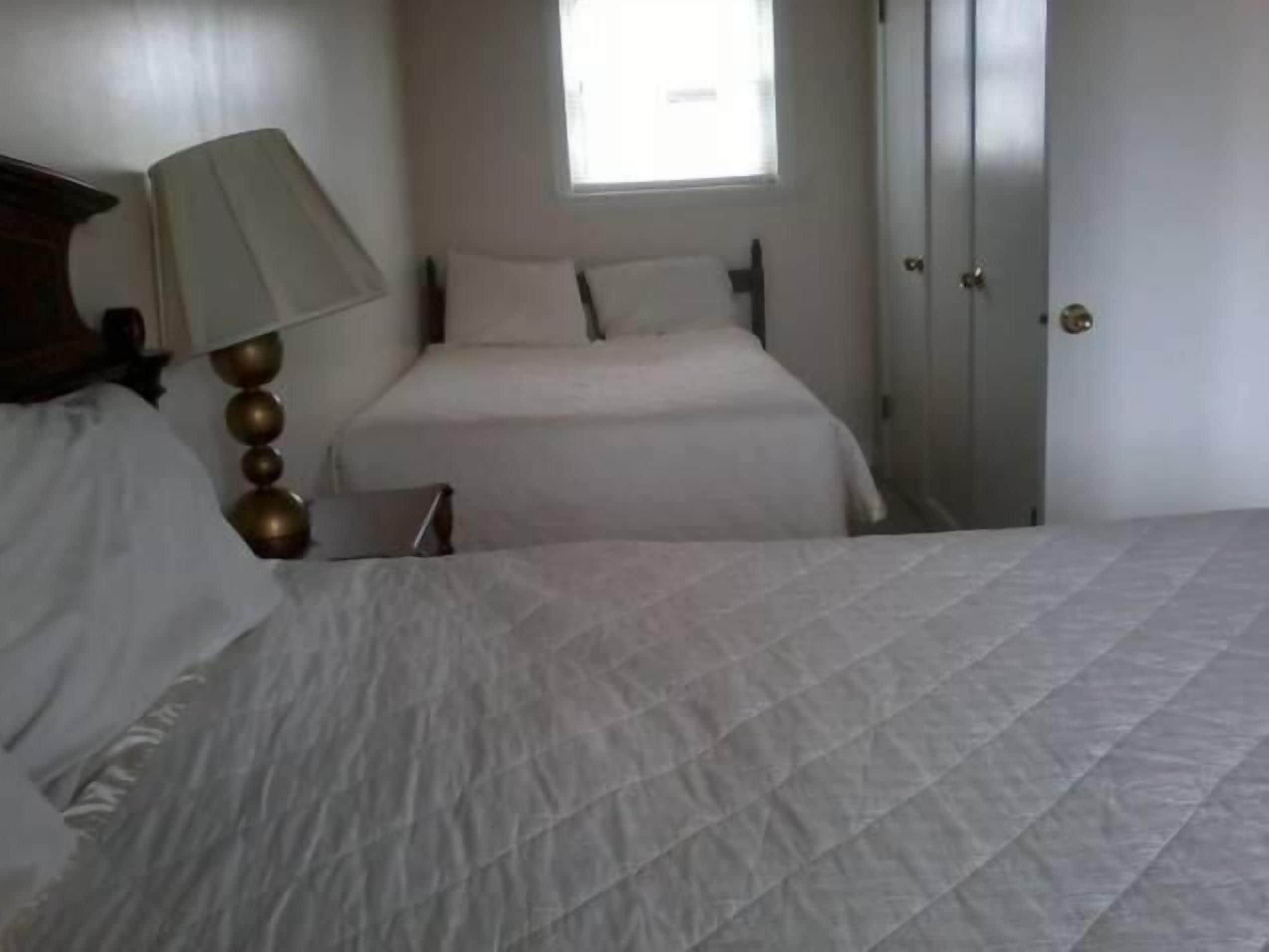 Quarto com cama, mesa de cabeceira com abajur, janela e porta.