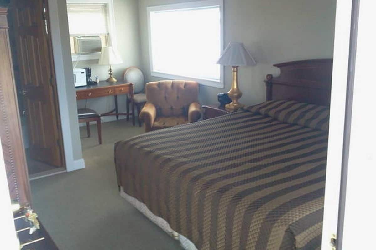 Quarto de hotel com cama, escrivaninha, cadeira, luminária e janela.