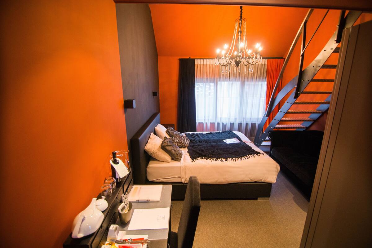 Quarto com cama, escrivaninha, cadeira, candelabro e escada.