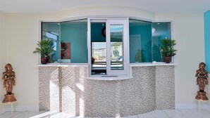 Uma área de recepção com um balcão curvo, uma porta de vidro e duas plantas em vasos.