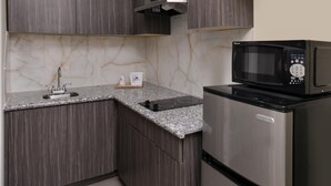 Uma cozinha com armários de madeira escura, bancada de granito, geladeira de aço inoxidável e micro-ondas preto.