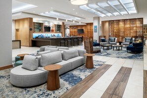 Um saguão de hotel moderno com área de bar, assentos e uma tela grande.