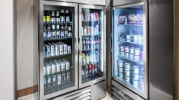 Unidade de refrigeração comercial com várias prateleiras repletas de bebidas e lanches.