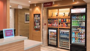 Uma área de recepção de hotel com um letreiro 'Check-in e Checkout Móvel', uma seção 'Em Caso de Necessidade' e geladeiras Towneplace Suites abastecidas com bebidas.