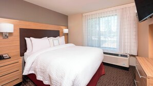 Quarto de hotel com uma cama grande, duas mesas de cabeceira, uma televisão de tela plana, um aparelho de ar condicionado e uma janela com cortinas.