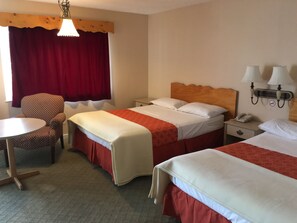 Quarto de hotel com duas camas, uma cadeira, uma mesa e uma luminária.