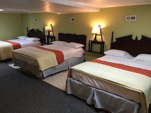 Quarto de hotel com três camas, cada uma com cabeceira e abajures.