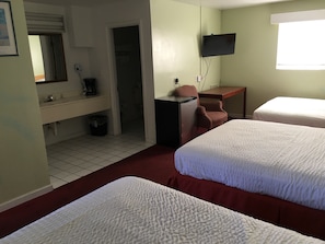 Quarto de hotel com duas camas, uma mesa, uma cadeira, uma televisão e banheiro.