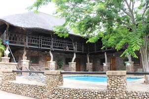 Um edifício com piscina, paredes de pedra e telhado de palha.