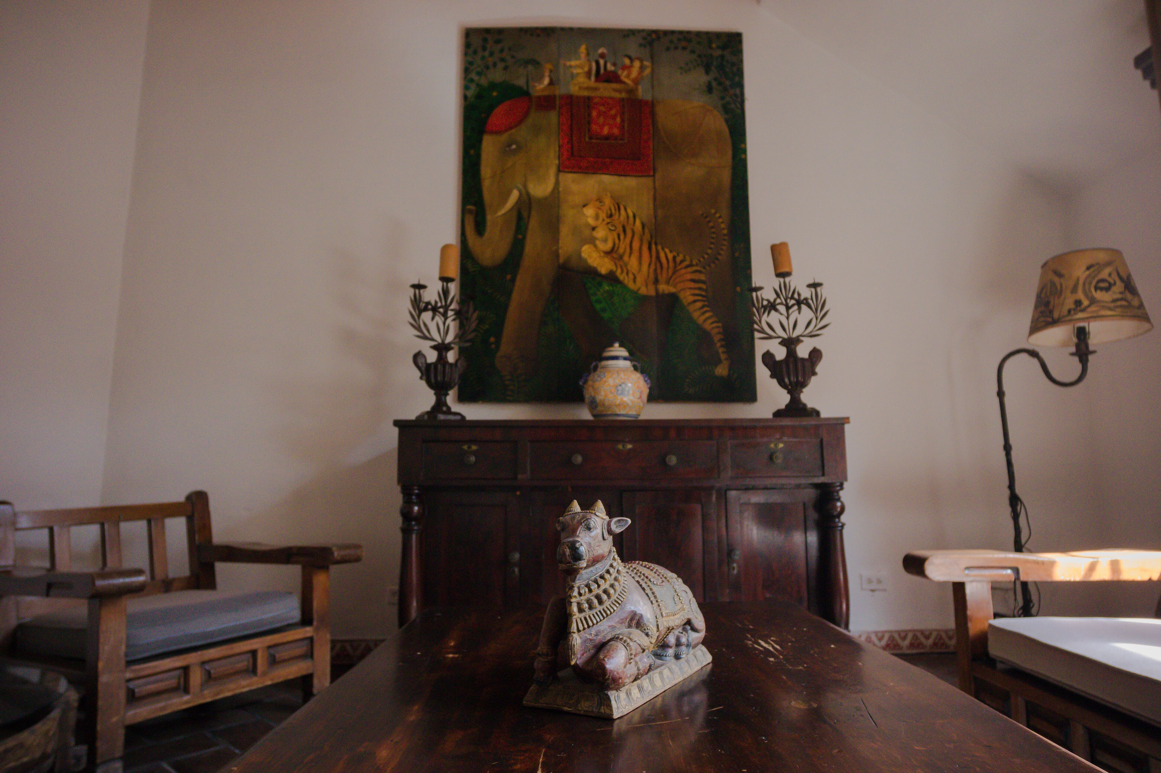 Um quarto com uma mesa de madeira, um quadro decorativo de elefante, uma pequena estatueta de elefante e um abajur.