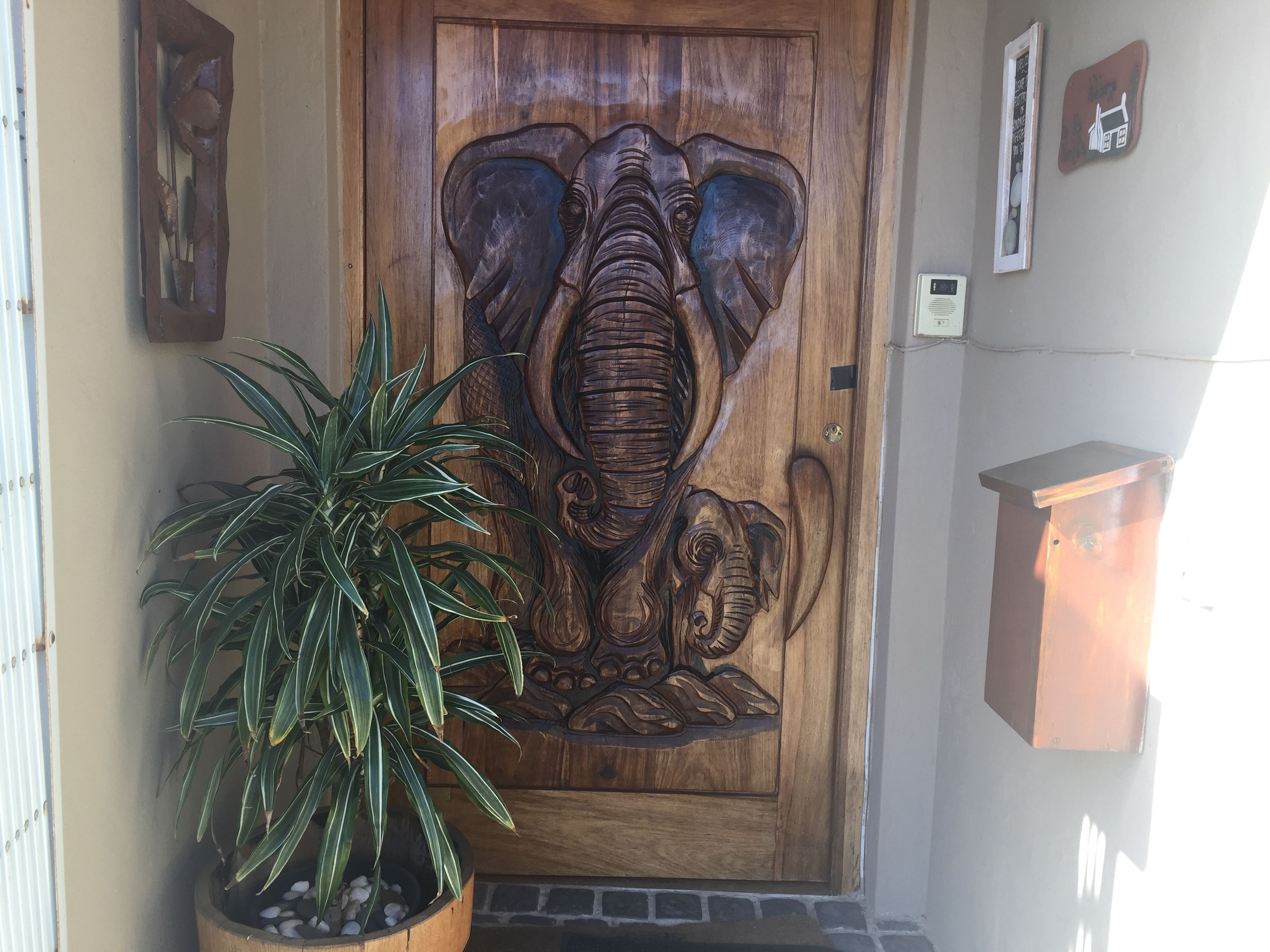 Uma porta de madeira com um entalhe de elefante, um vaso de planta e um pequeno armário.