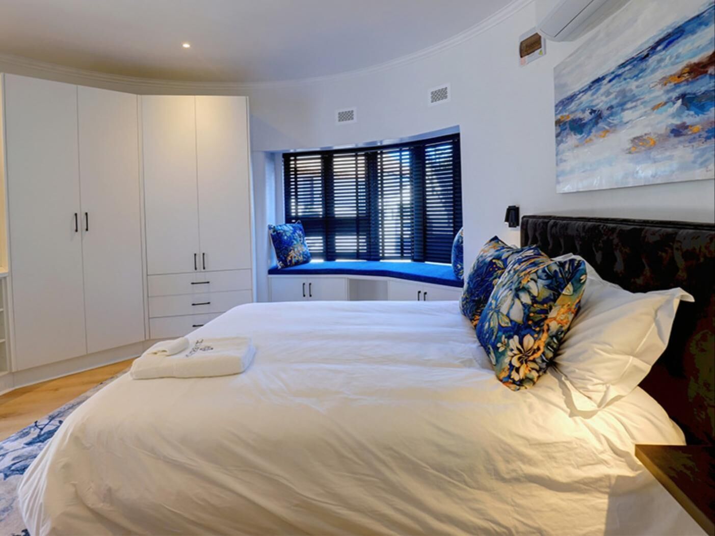 Quarto com uma cama grande, um banco embutido com assento, uma janela com persianas e um quadro na parede.