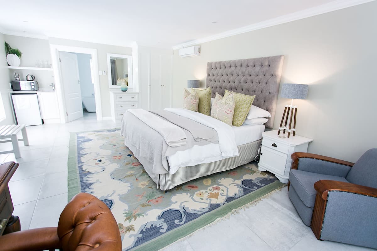 Quarto com cama grande, mesa de cabeceira, cadeira e escrivaninha com abajur.