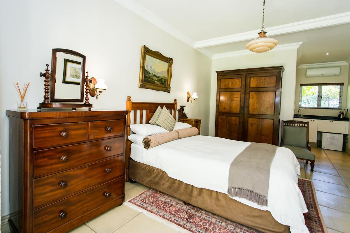 Quarto com cômoda de madeira, cama com colcha branca e marrom, pintura na parede e guarda-roupa de madeira grande.