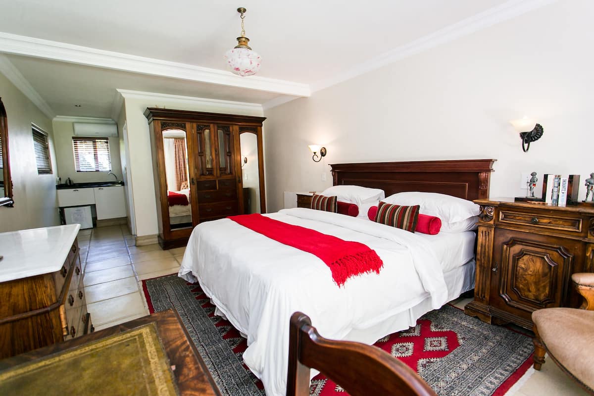 Quarto com uma cama grande, cabeceira de madeira e manta vermelha. Há uma cômoda de madeira e uma escrivaninha com uma cadeira.