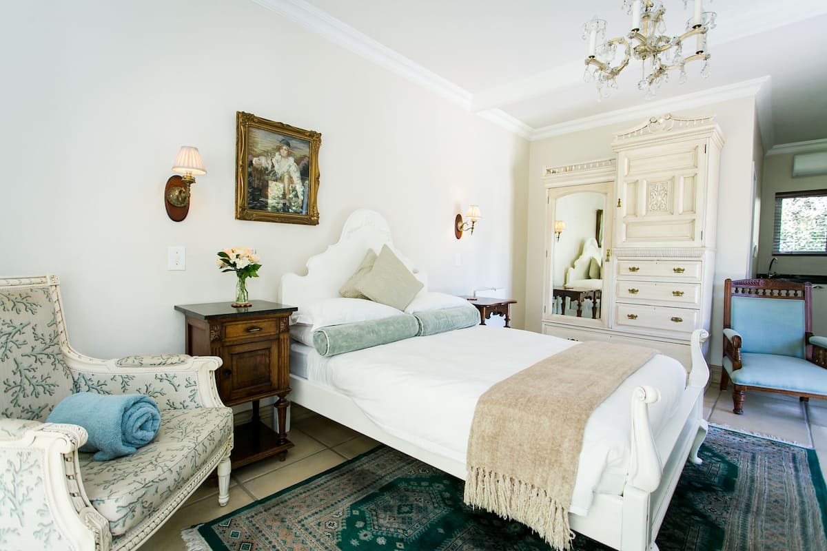 Quarto com uma cama grande, uma cadeira, cômoda, espelho e lustre.