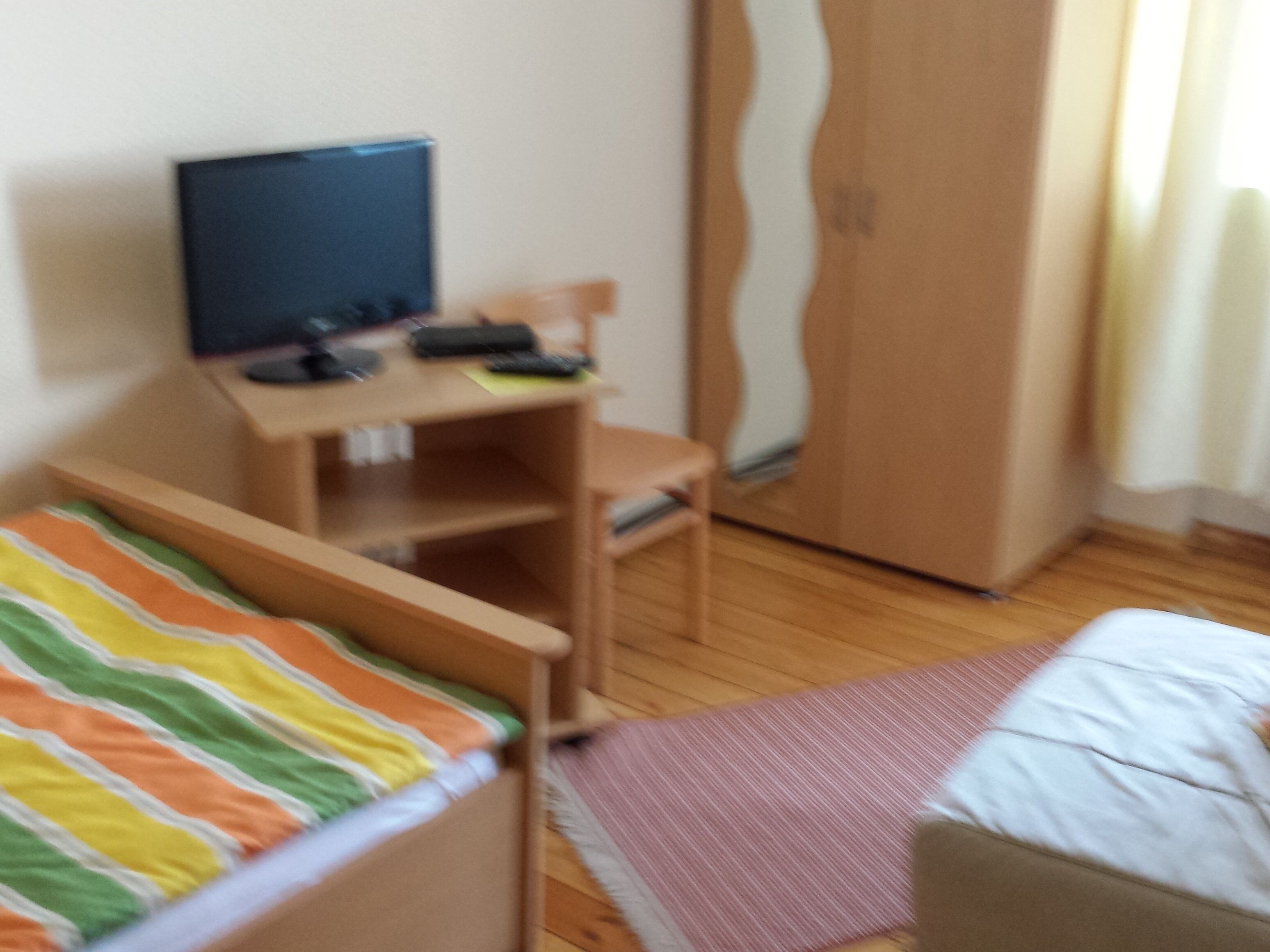 Um quarto com uma cama, uma escrivaninha com computador, uma cadeira e um guarda-roupa.