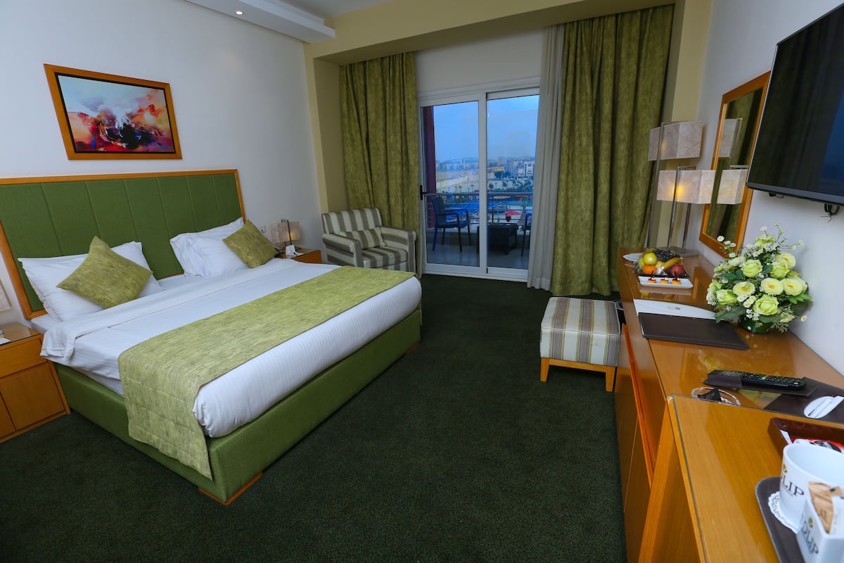 Quarto de hotel com uma cama grande, uma escrivaninha com computador, uma cadeira, televisão e varanda com vista.
