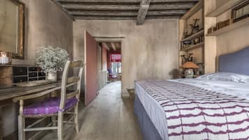 Quarto com escrivaninha de madeira, cadeira, cama com roupa de cama estampada e prateleira com diversos objetos.
