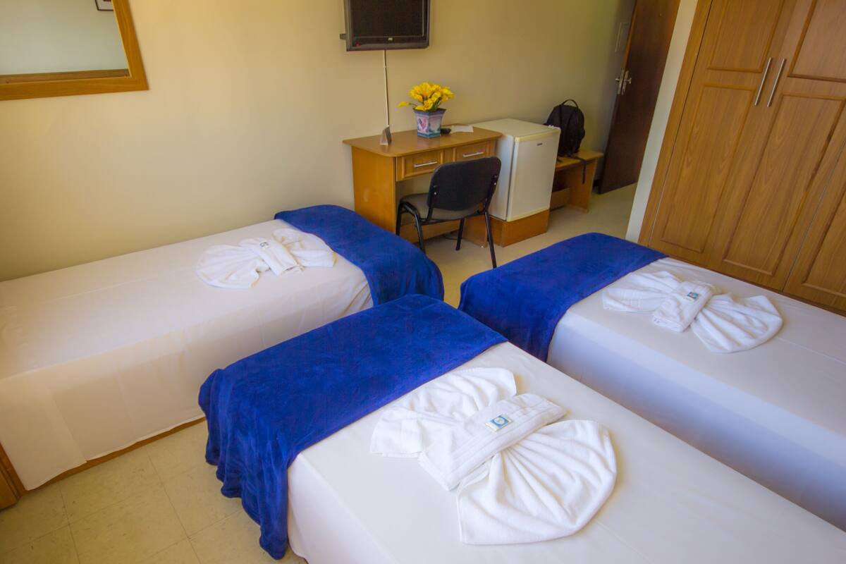 Quarto de hotel com duas camas de solteiro, uma escrivaninha com computador, uma cadeira e um guarda-roupa.