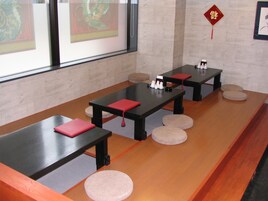 Um quarto com várias mesas e cadeiras dispostas em fila. Há objetos decorativos nas mesas e um quadro na parede.