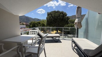 Uma varanda com mesa e cadeiras, um sofá e vista para montanhas e árvores.