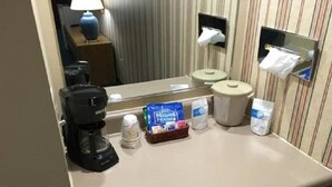 Casa de banho de hotel com lavatório, máquina de café, caixa de lenços de papel e lixeira.