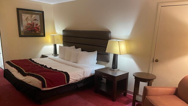 Quarto de hotel com uma cama, duas mesas de cabeceira com abajures, uma cadeira e uma porta.