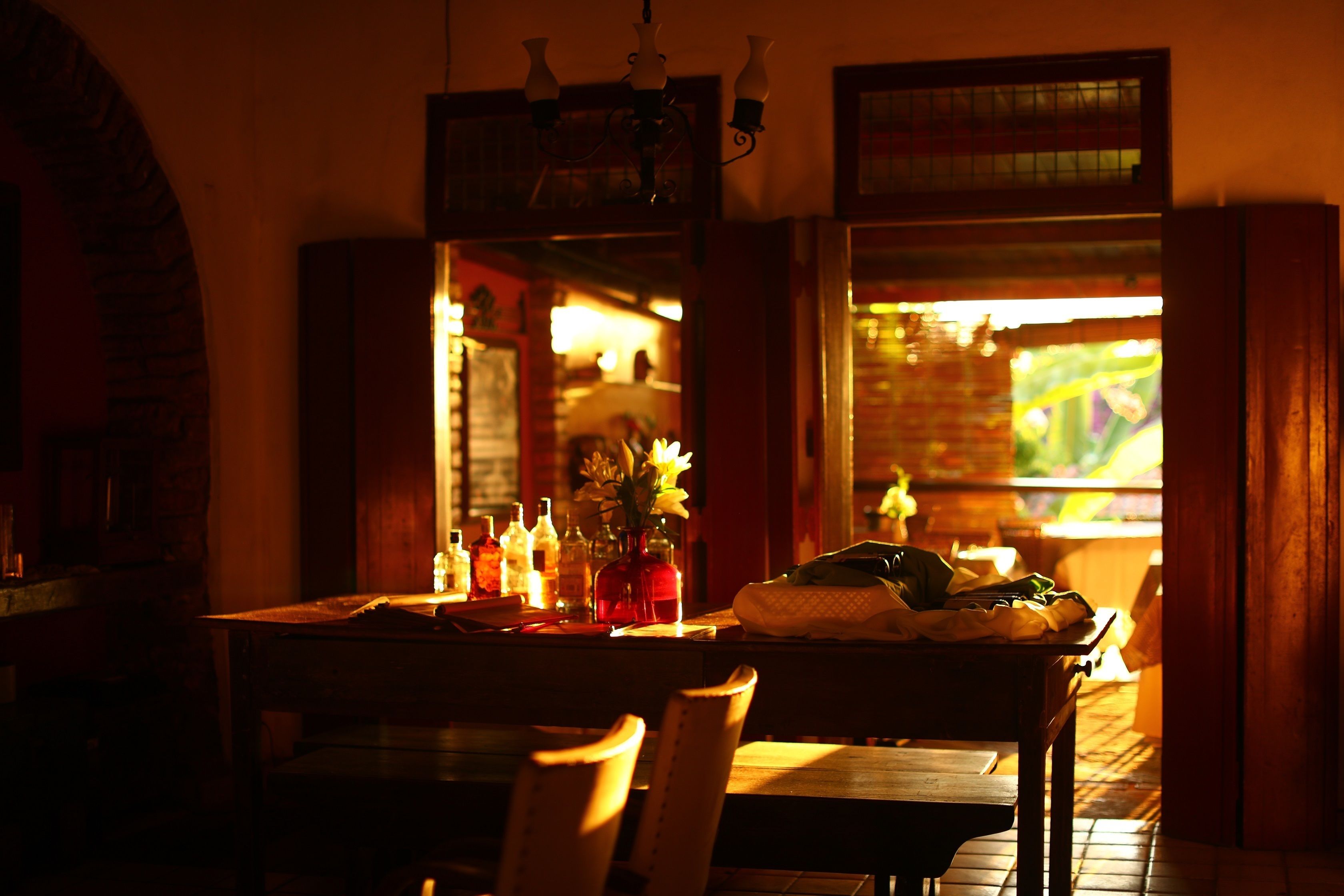 Uma sala de jantar bem iluminada, com uma mesa de madeira, cadeiras e diversos frascos e flores sobre a mesa.