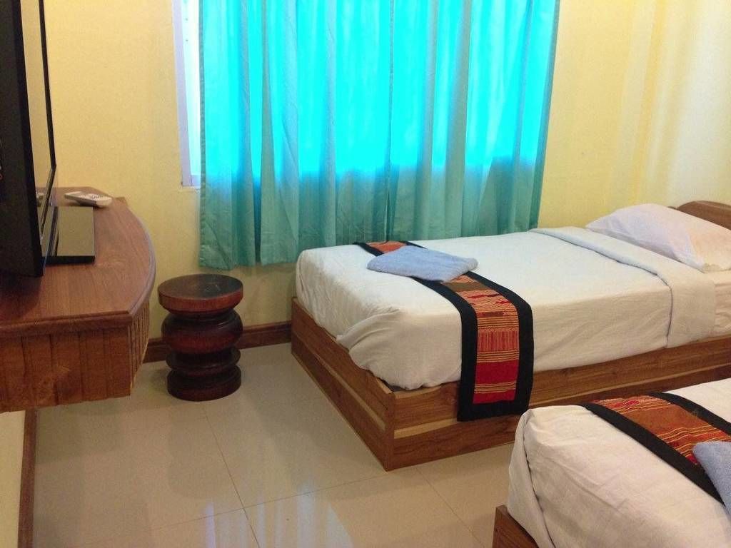 Quarto de hotel com duas camas de madeira, uma mesinha de cabeceira de madeira e uma televisão à esquerda.