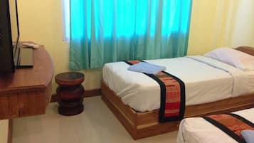 Quarto de hotel com duas camas de madeira, uma mesinha de cabeceira de madeira e uma televisão à esquerda.