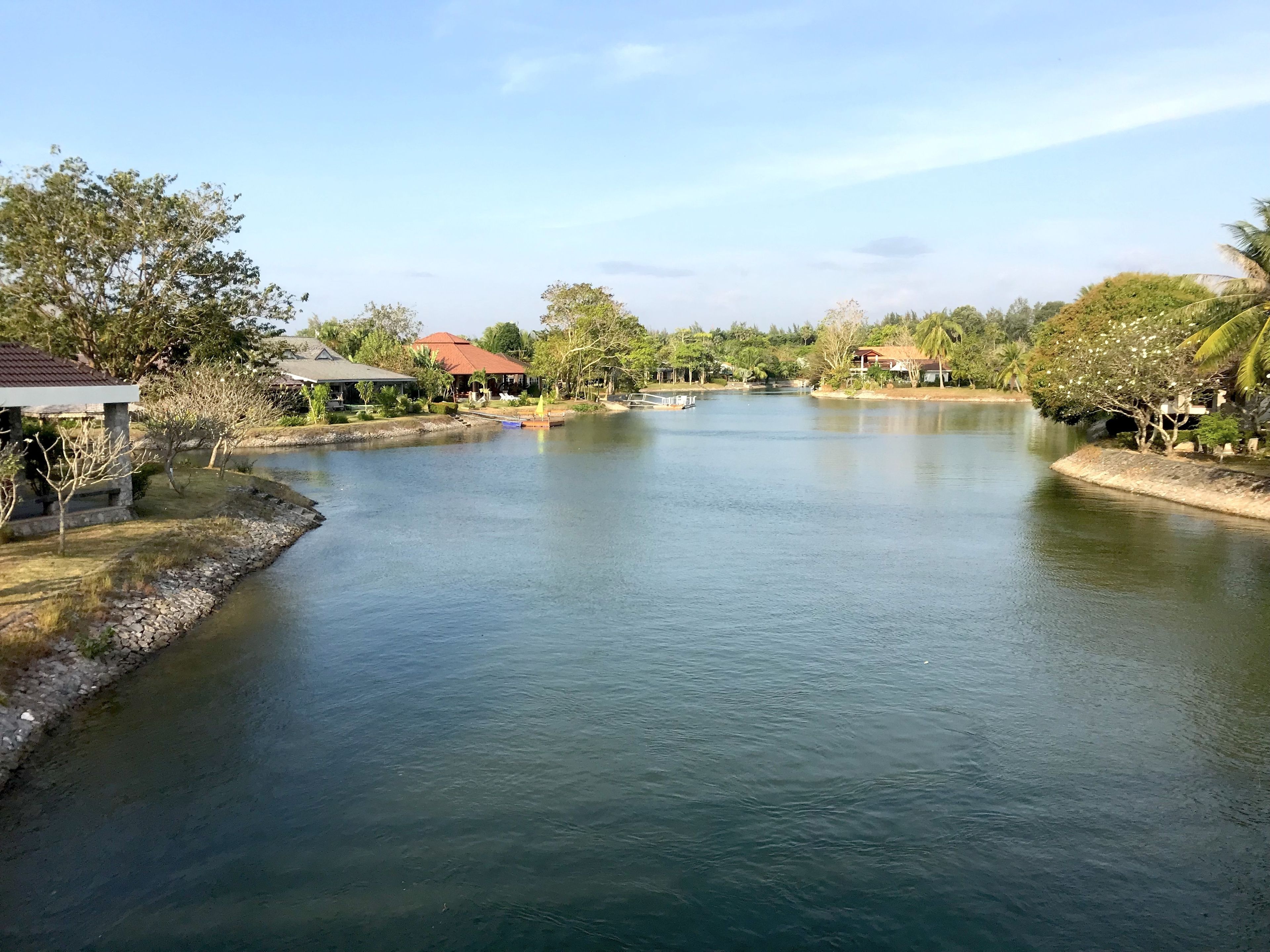 Um rio calmo com casas em ambas as margens, rodeado por árvores e vegetação.