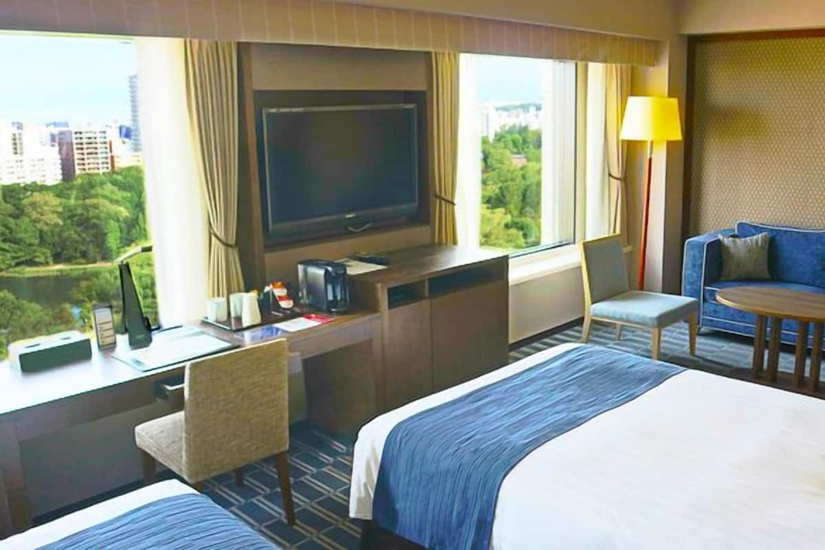 Quarto de hotel com cama, escrivaninha com televisão, sofá e vista para a cidade.