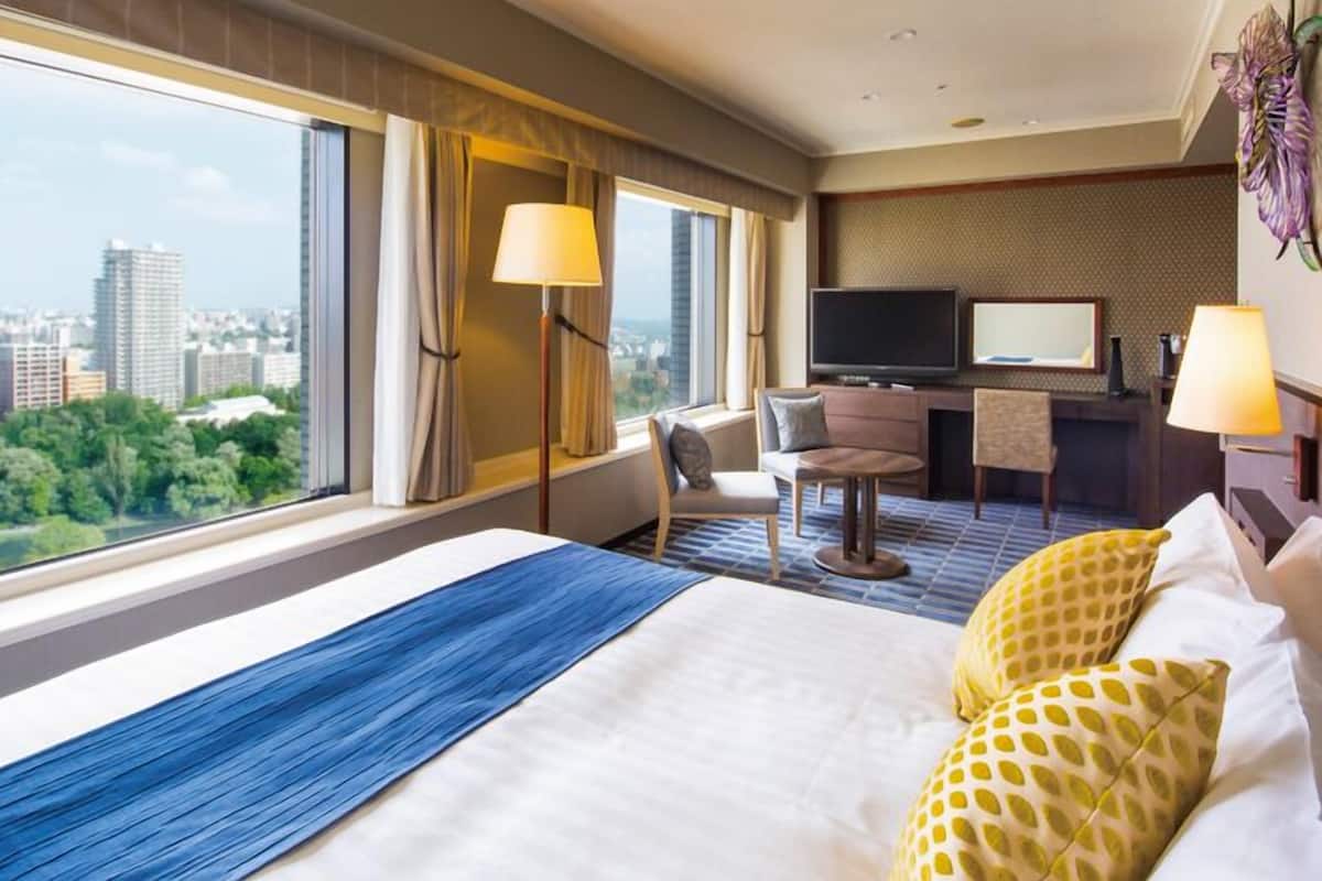 Quarto de hotel com cama grande, escrivaninha, cadeira, televisão e vista para a cidade.
