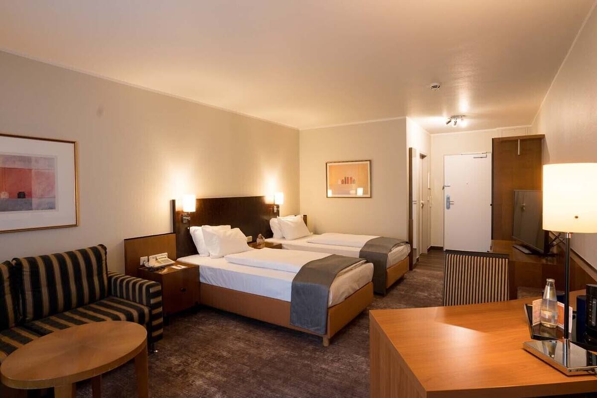 Quarto de hotel com duas camas, um sofá, uma escrivaninha e uma televisão.