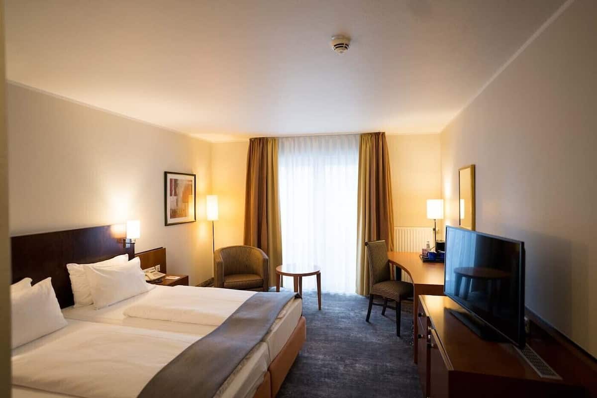 Quarto de hotel com uma cama grande, uma escrivaninha com televisão, uma cadeira e uma pequena mesa.