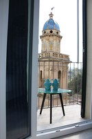 Varanda com mesa de vidro e dois objetos decorativos, com vista para um edifício histórico com cúpula e arquitetura detalhada.
