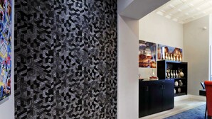 Um interior moderno com parede estampada em padrão geométrico, um armário de madeira escura com objetos decorativos e uma cadeira vermelha.