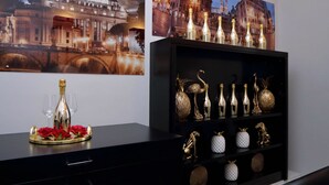 Uma prateleira preta com garrafas decorativas e vasos, uma garrafa de vinho com copos e um tabuleiro com rosas vermelhas.