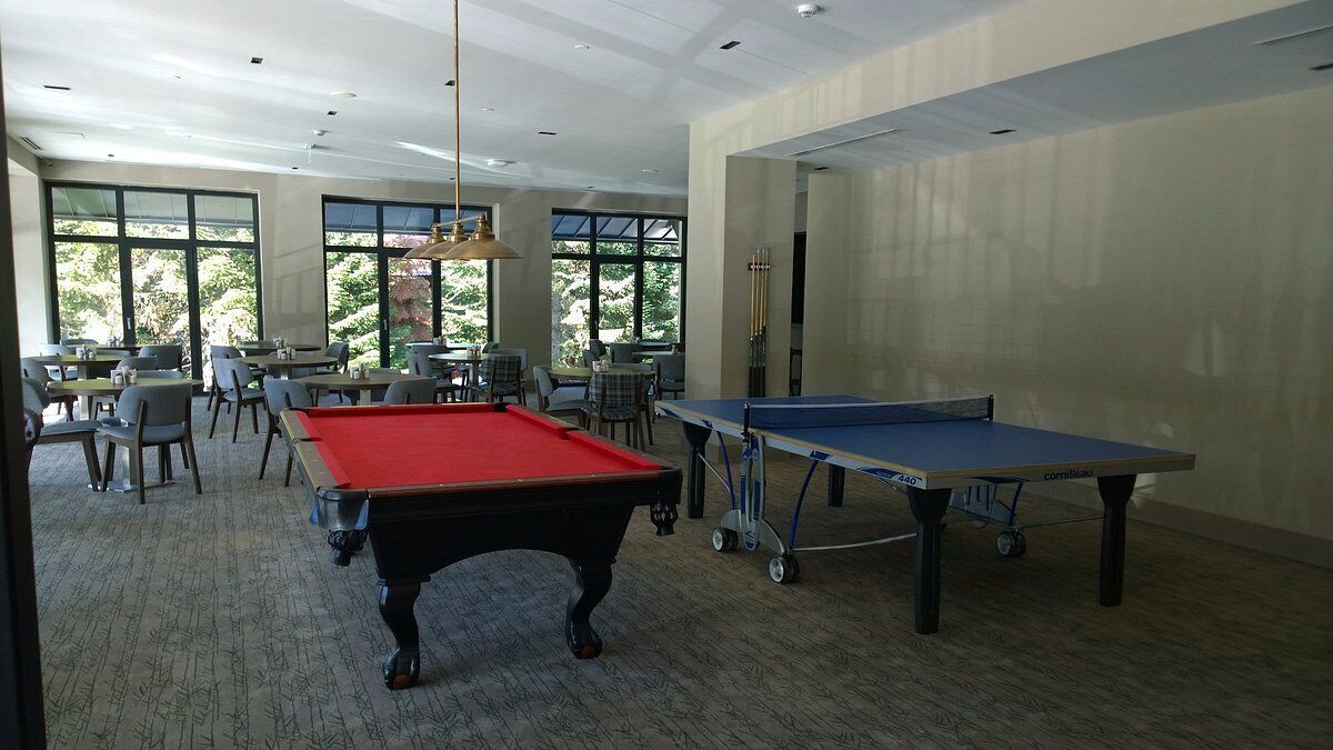 Uma sala de bilhar com mesa de bilhar, mesa de pingue-pongue e vários cadeiras e mesas.