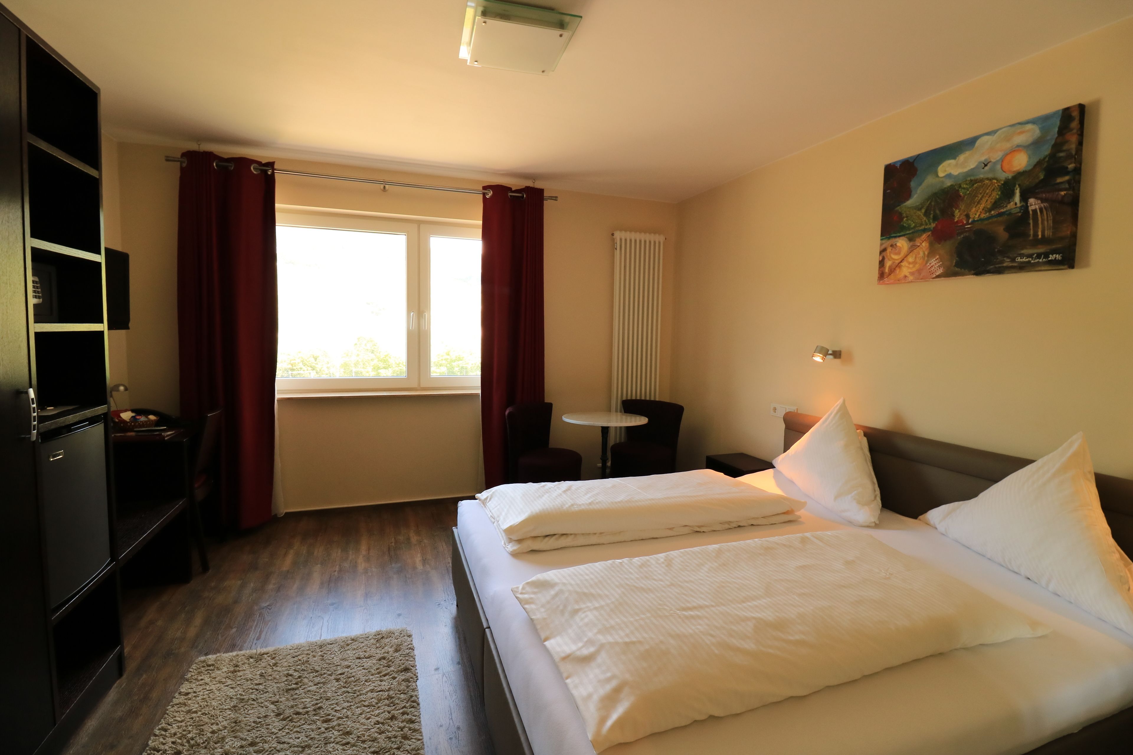 Quarto de hotel com cama, escrivaninha, cadeira, mesa pequena e um quadro na parede.