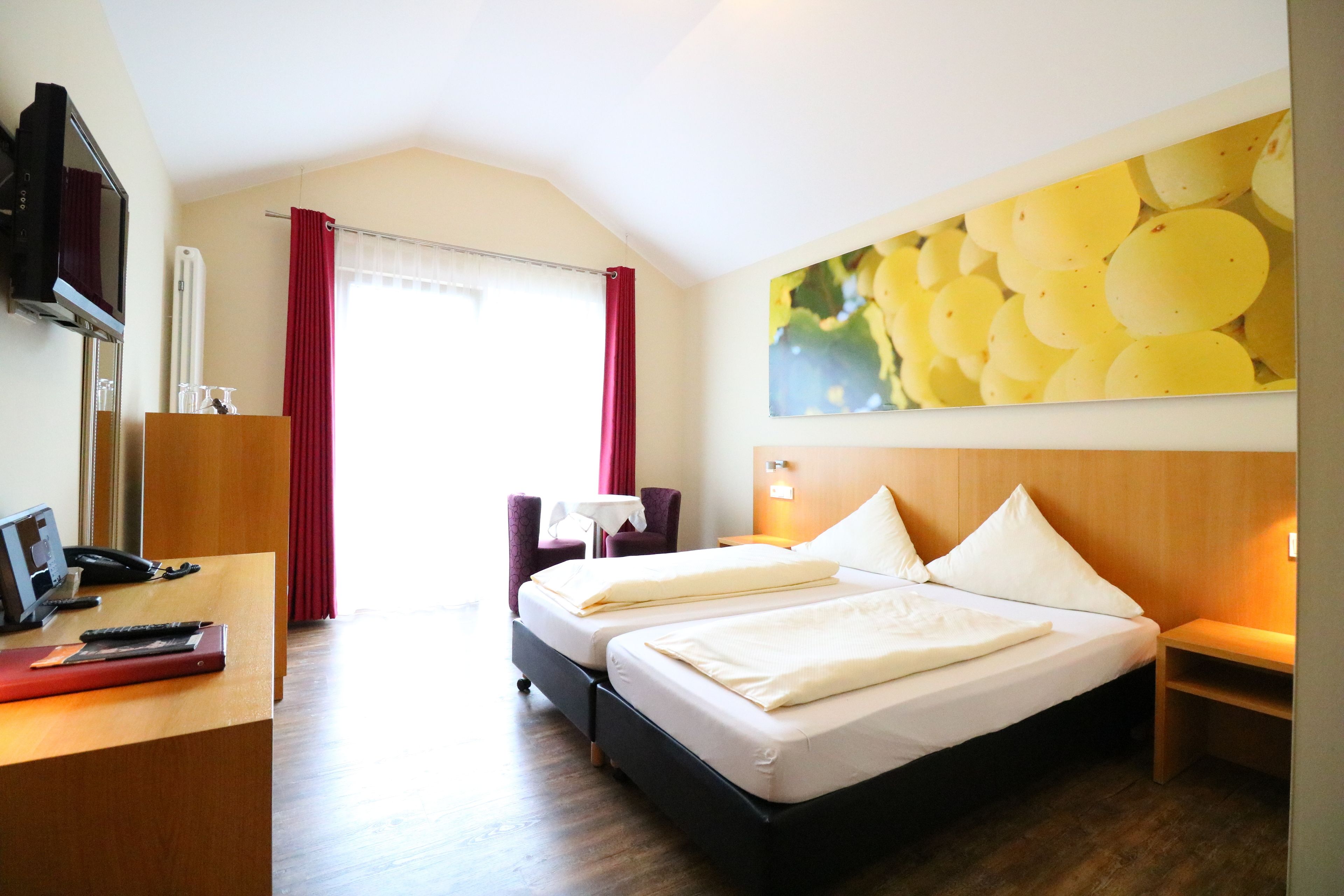 Quarto de hotel com duas camas, uma escrivaninha com telefone e uma janela grande com cortinas.