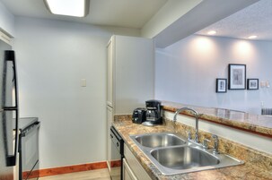 Uma cozinha compacta com bancada de granito, pia de aço inoxidável e cafeteira.
