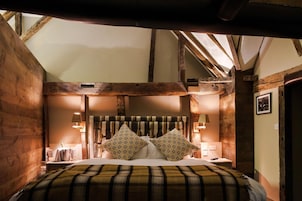 Um quarto aconchegante com teto de madeira, uma cama com roupa de cama xadrez e duas luminárias de cabeceira.