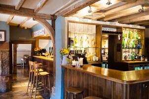 Uma área de bar com vigas de madeira, banquetas e diversas garrafas de bebidas.