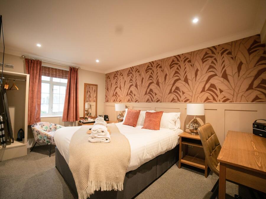 Quarto de hotel com uma cama grande, uma secretária com cadeira, uma televisão e um guarda-roupa.