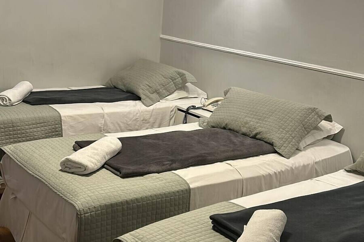 Duas camas de solteiro com roupa de cama acolchoada, uma luminária de cabeceira e um telefone na parede.