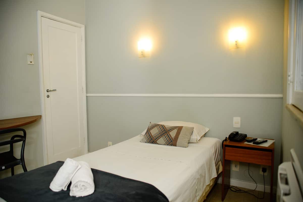 Quarto de hotel com cama, escrivaninha e duas luminárias.