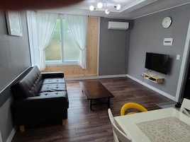 Sala de estar com sofá, mesa de centro, televisão e janela com cortinas.